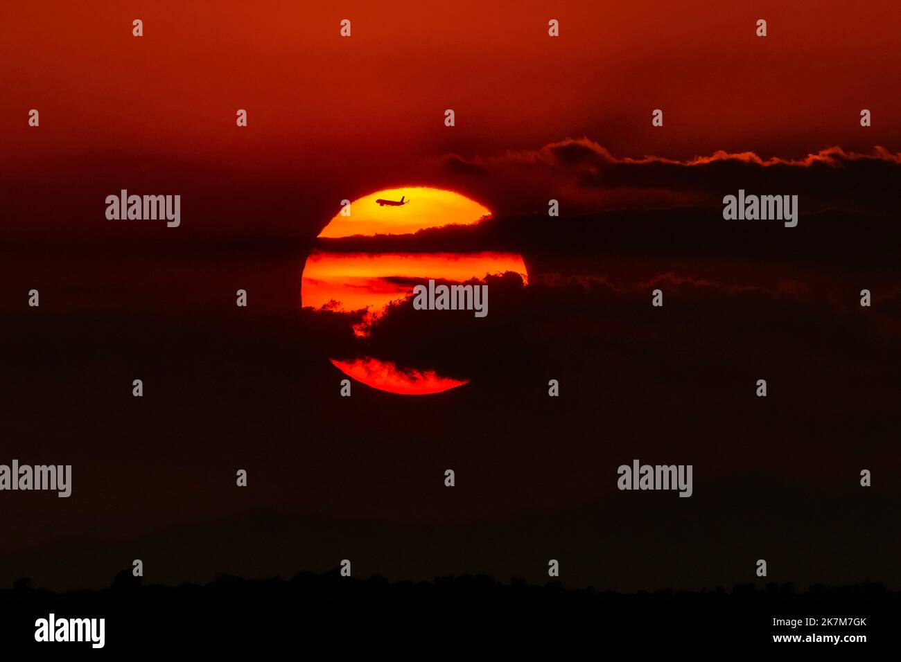 Red sun setting partly obscured by some clouds with an airplane ...