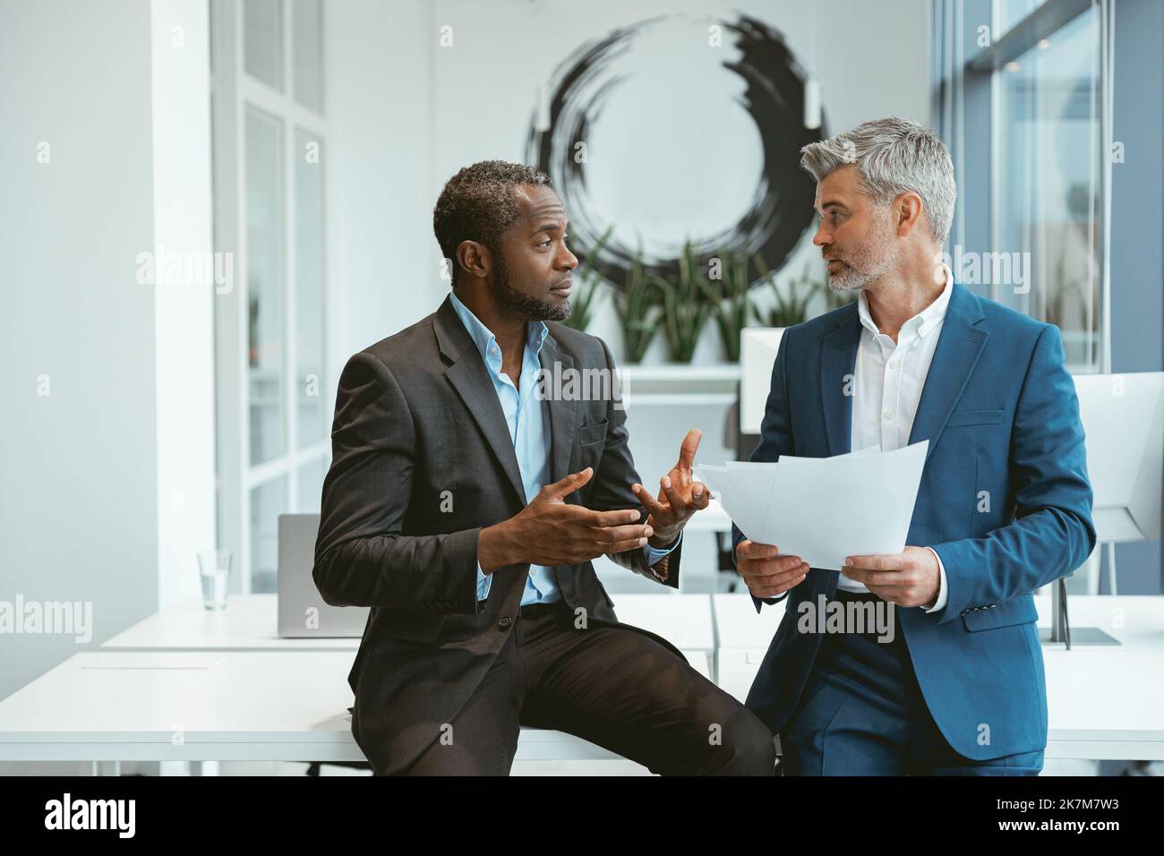 Two businessmen talking about deal sitting in meeting room in modern ...