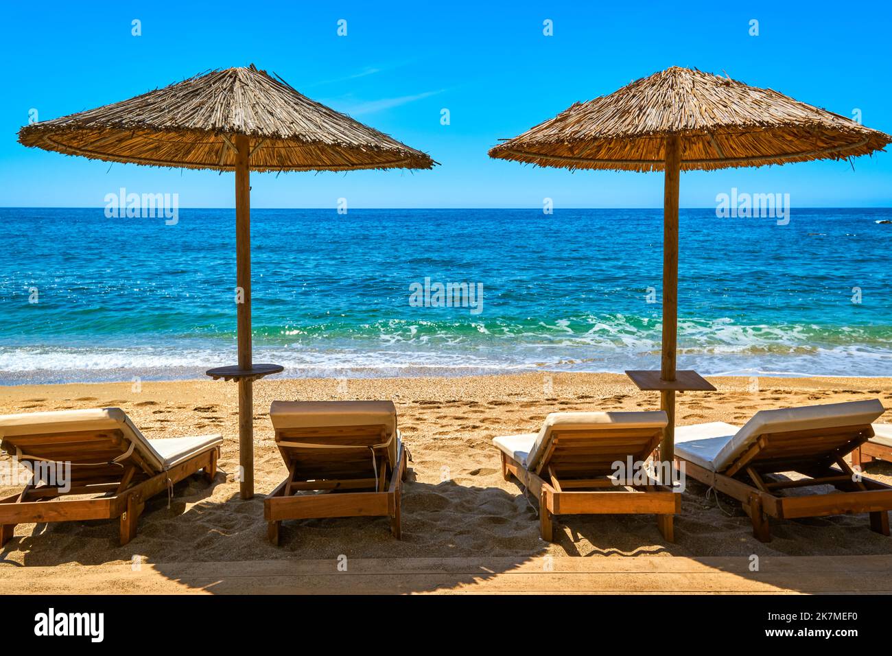 Two sun umbrellas and four sunbeds ready for tourists on sandy beach. Summer sunshine, vacations ...