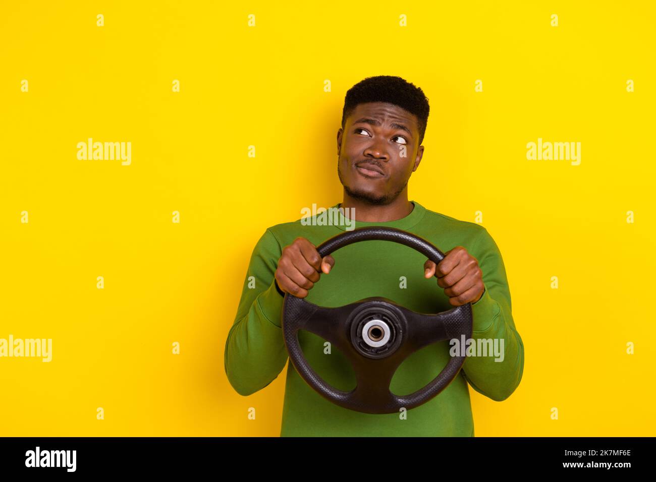 Portrait of attractive minded guy holding steering wheel thinking copy ...