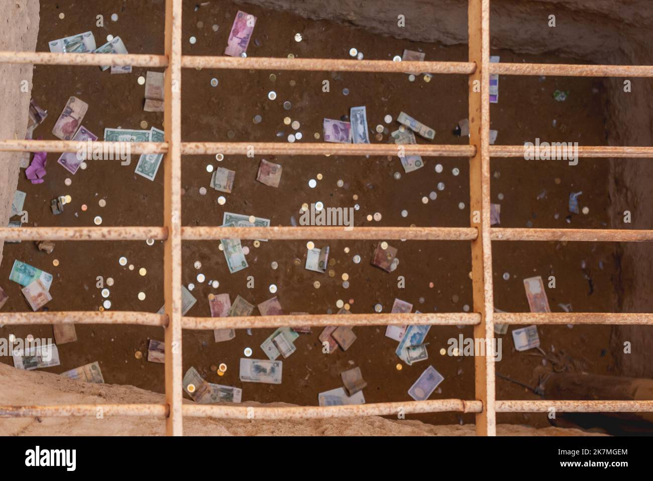 Different coins and banknotes in hole under iron bars. Tourists want to ...