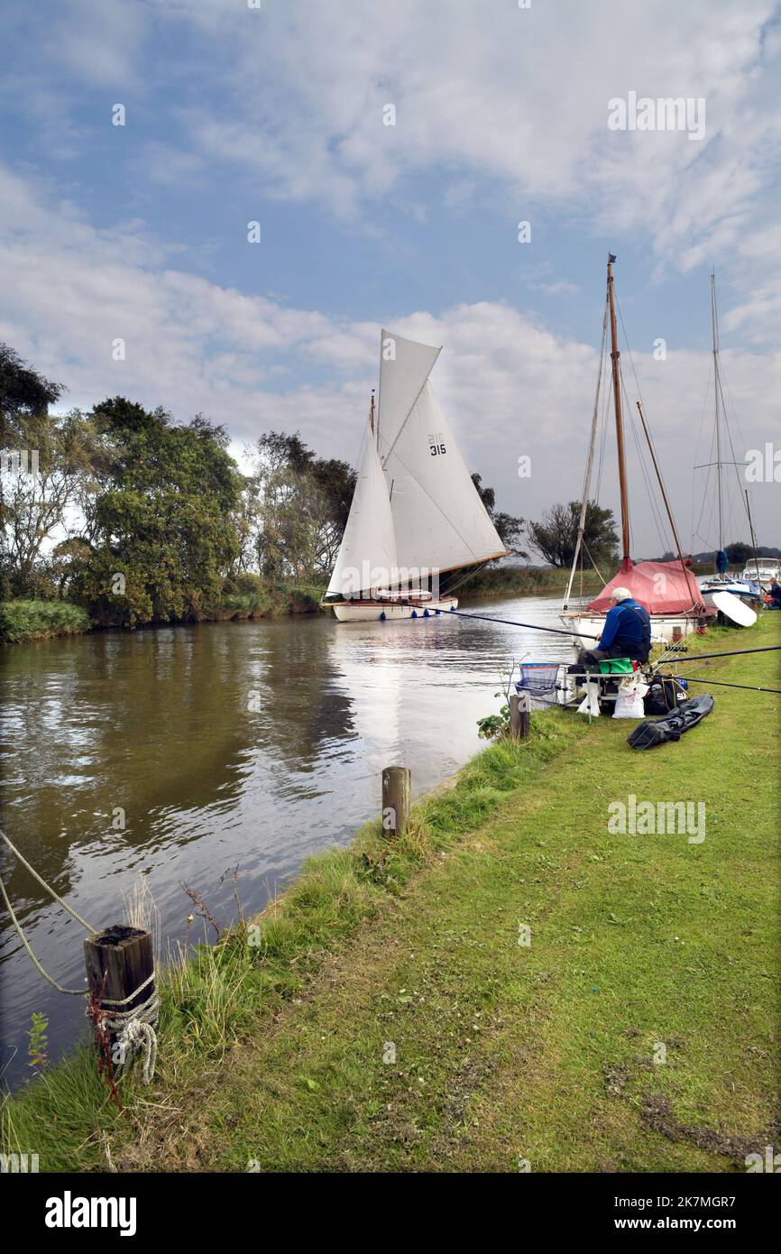match fisherman and traditional broads sailing boat on river thurne ...