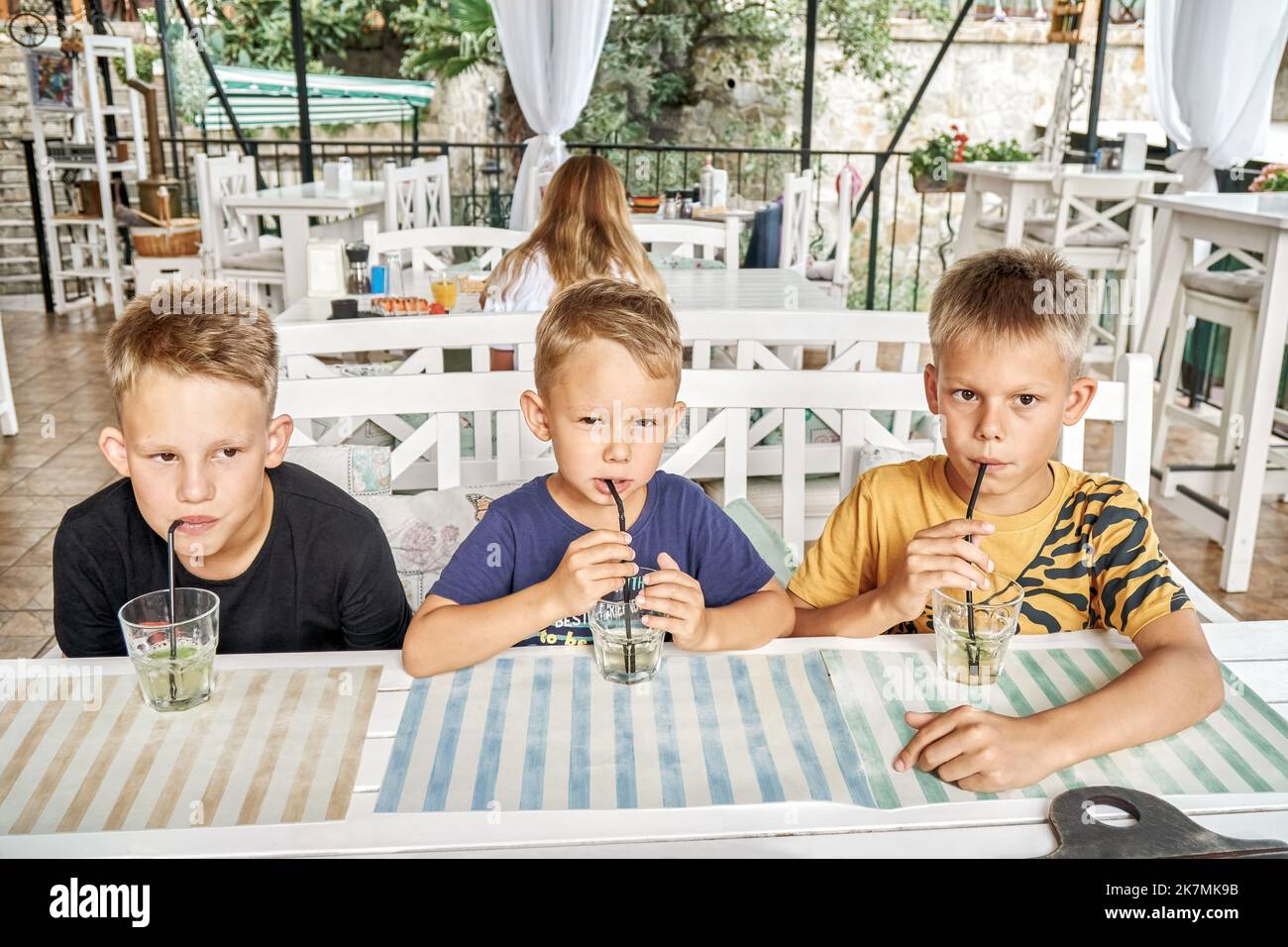 Brothers sit at wooden table in restaurant drinking lemonade from ...