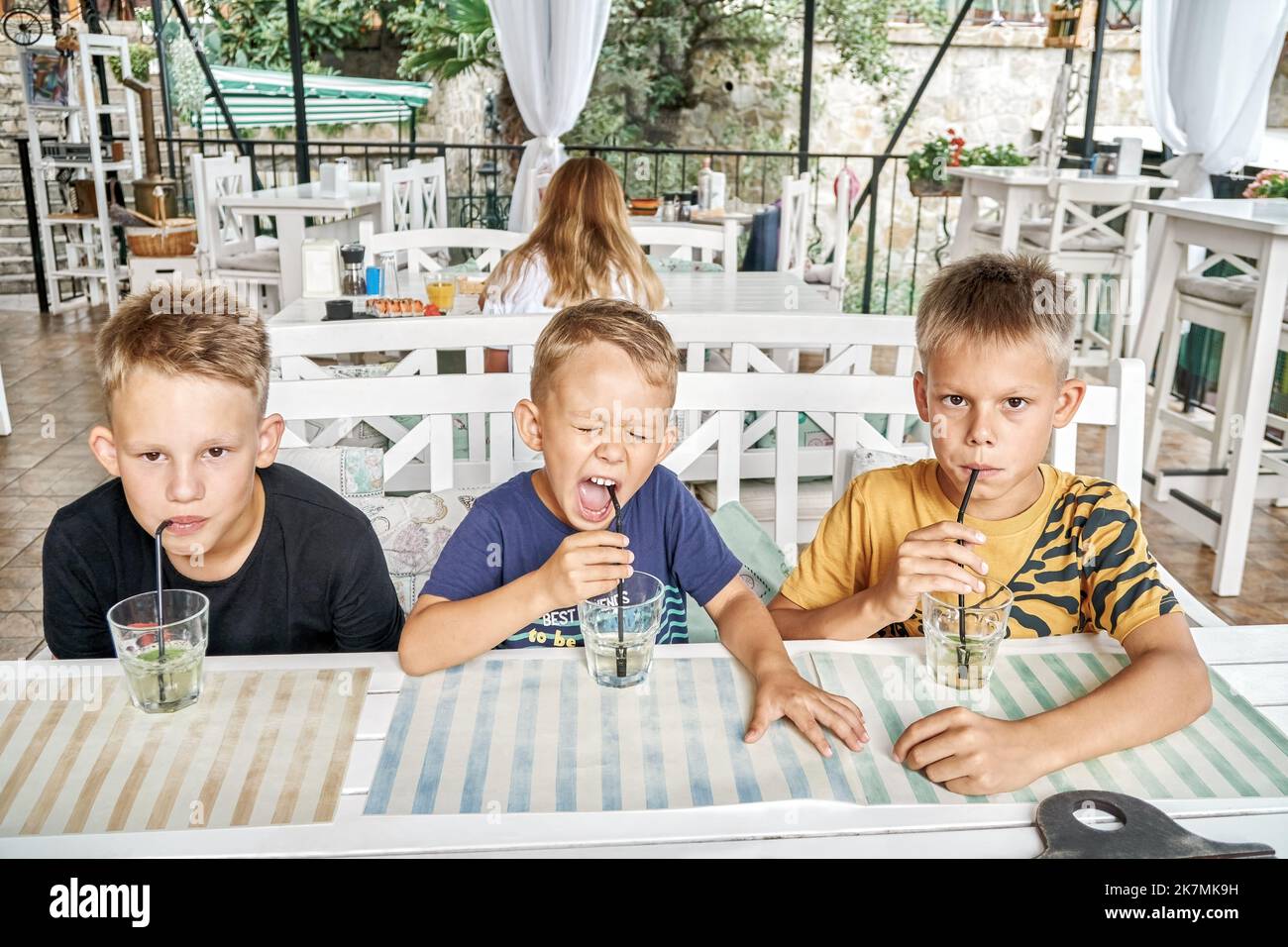 Brothers sit at wooden table in restaurant drinking lemonade from ...