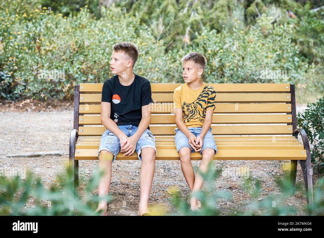Brothers sit on bench tired from long walk in park. Fair-haired boys ...