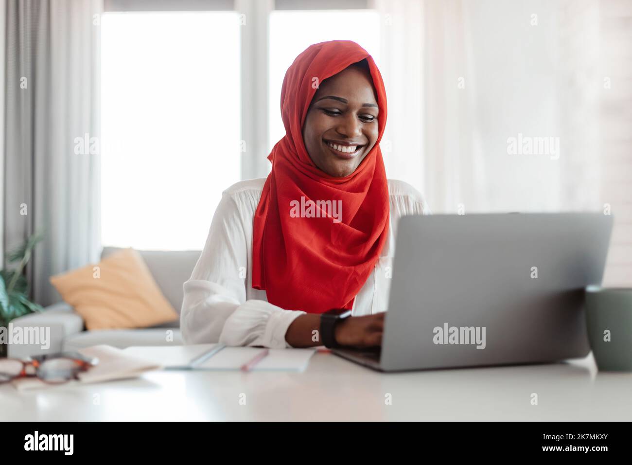 Remote job. Happy islamic woman in red hijab working on laptop, typing ...