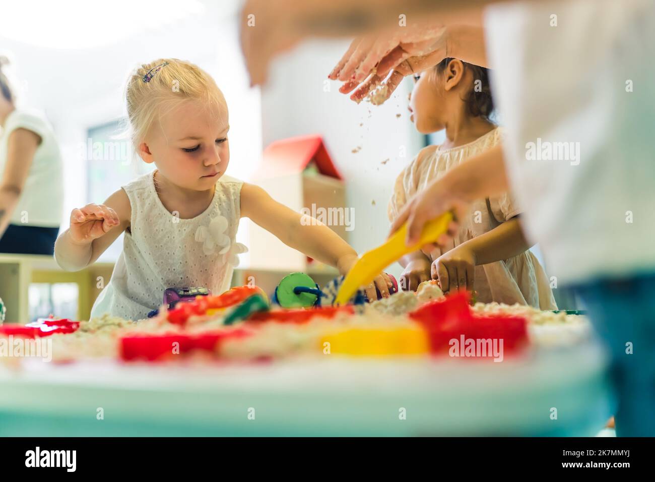 adorable blond little girl focusing on making figures with kinetic sand ...