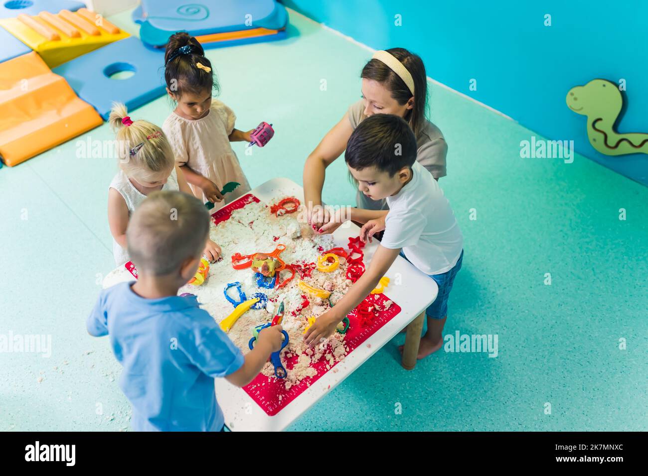 Caucasian kids and their young teacher making forms with kinetic sand ...
