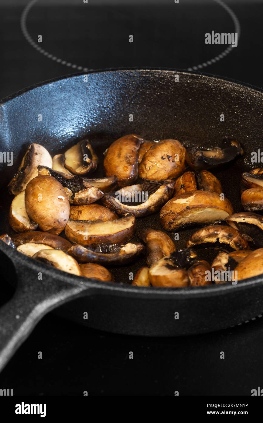 Frying chestnut mushrooms in a cast iron frying pan, on an electric hob ...