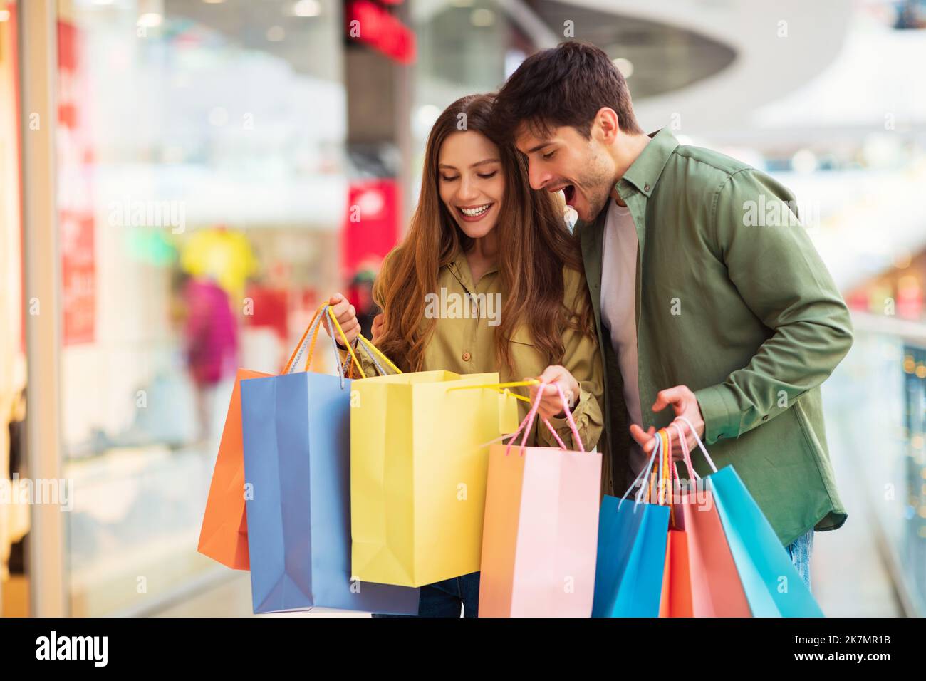 Excited Buyers Couple Looking Inside Shopping Bags In Modern ...