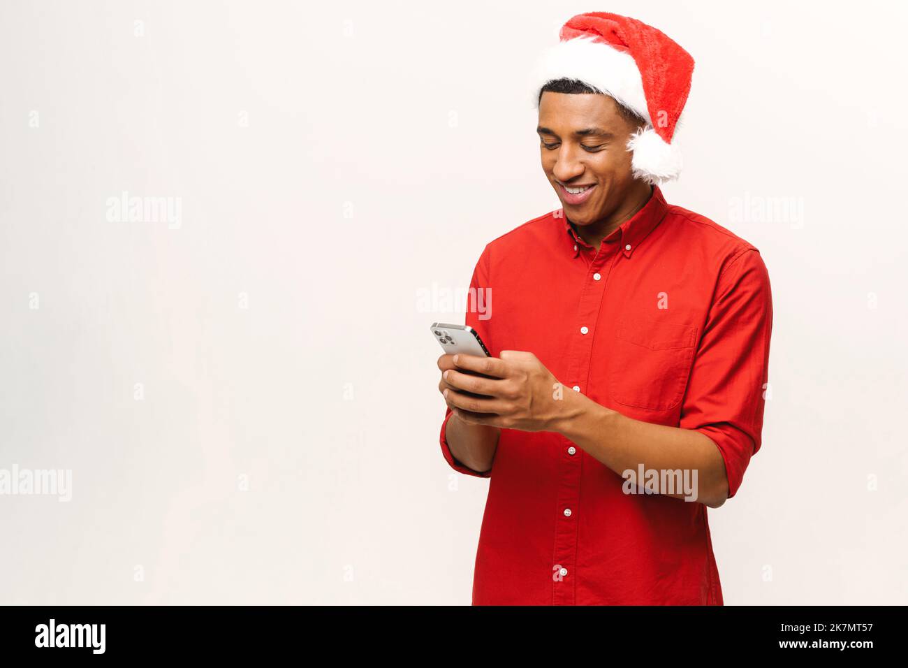 Cheerful attractive young man in santa hat holding smartphone, enjoying ...