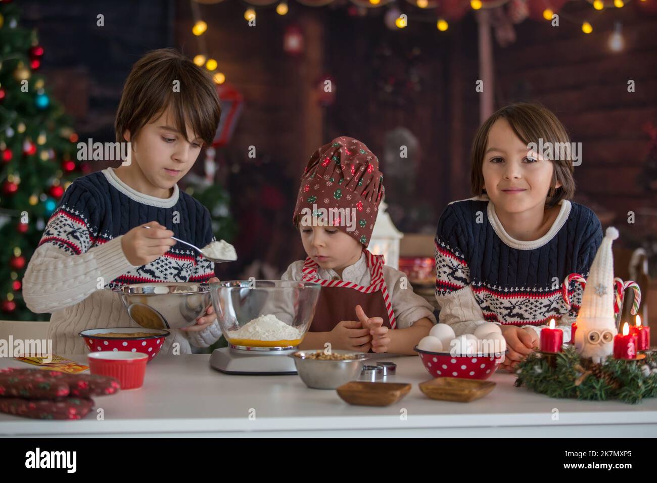 Cute blond child and his brothers, baking christmas cookies at home ...