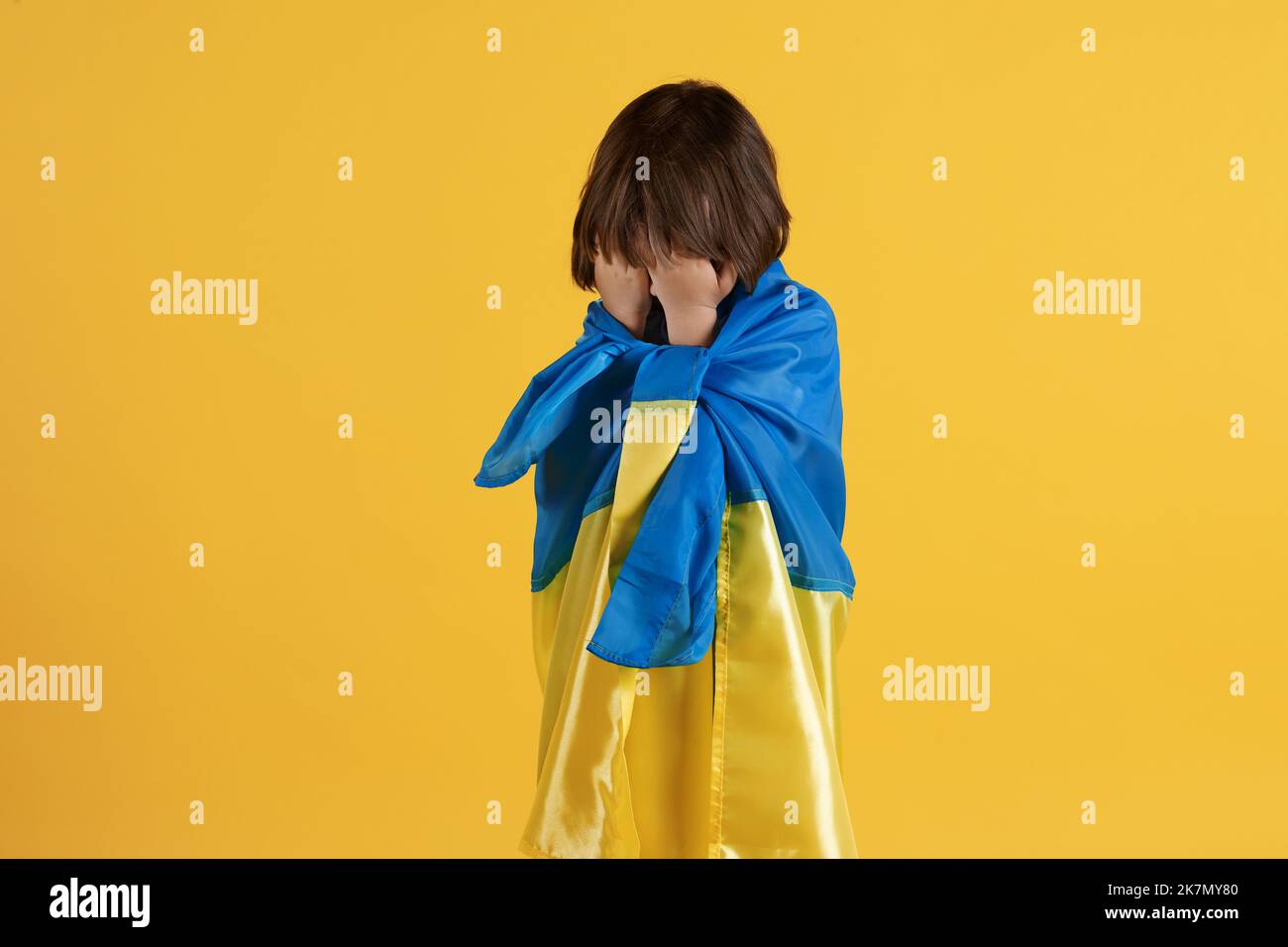 Unhappy little boy wrapped in Ukrainian flag crying, hiding face in ...