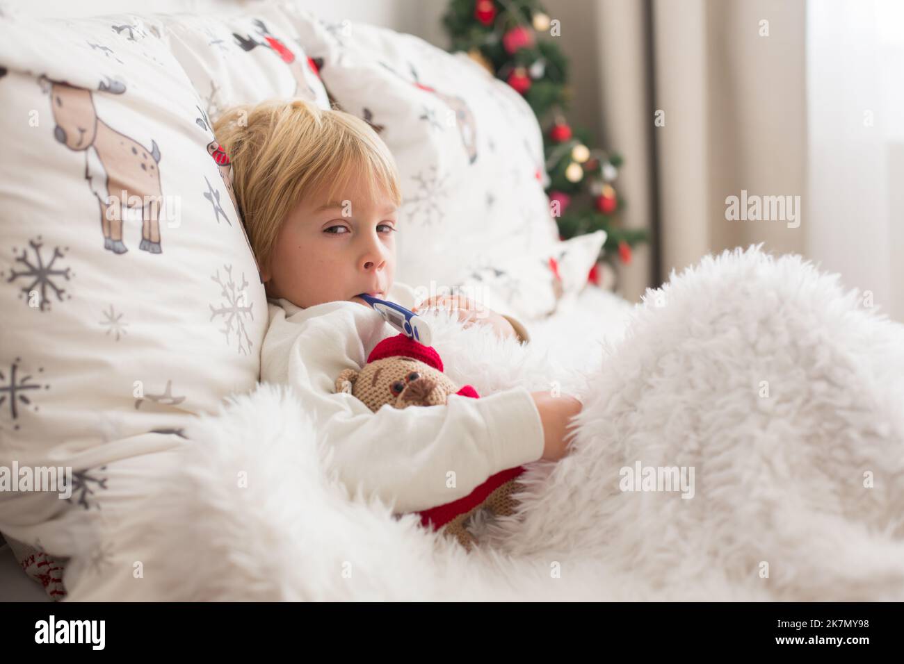 Beautiful blond toddler child, sick boy with fever, lying in bed on ...