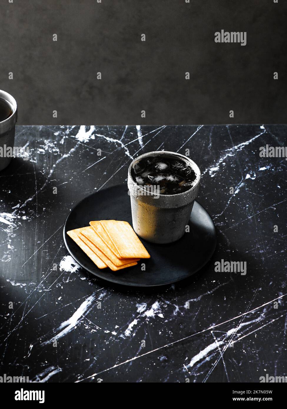 A vertical shot of crackers in a black plate and a steel cup with ice ...