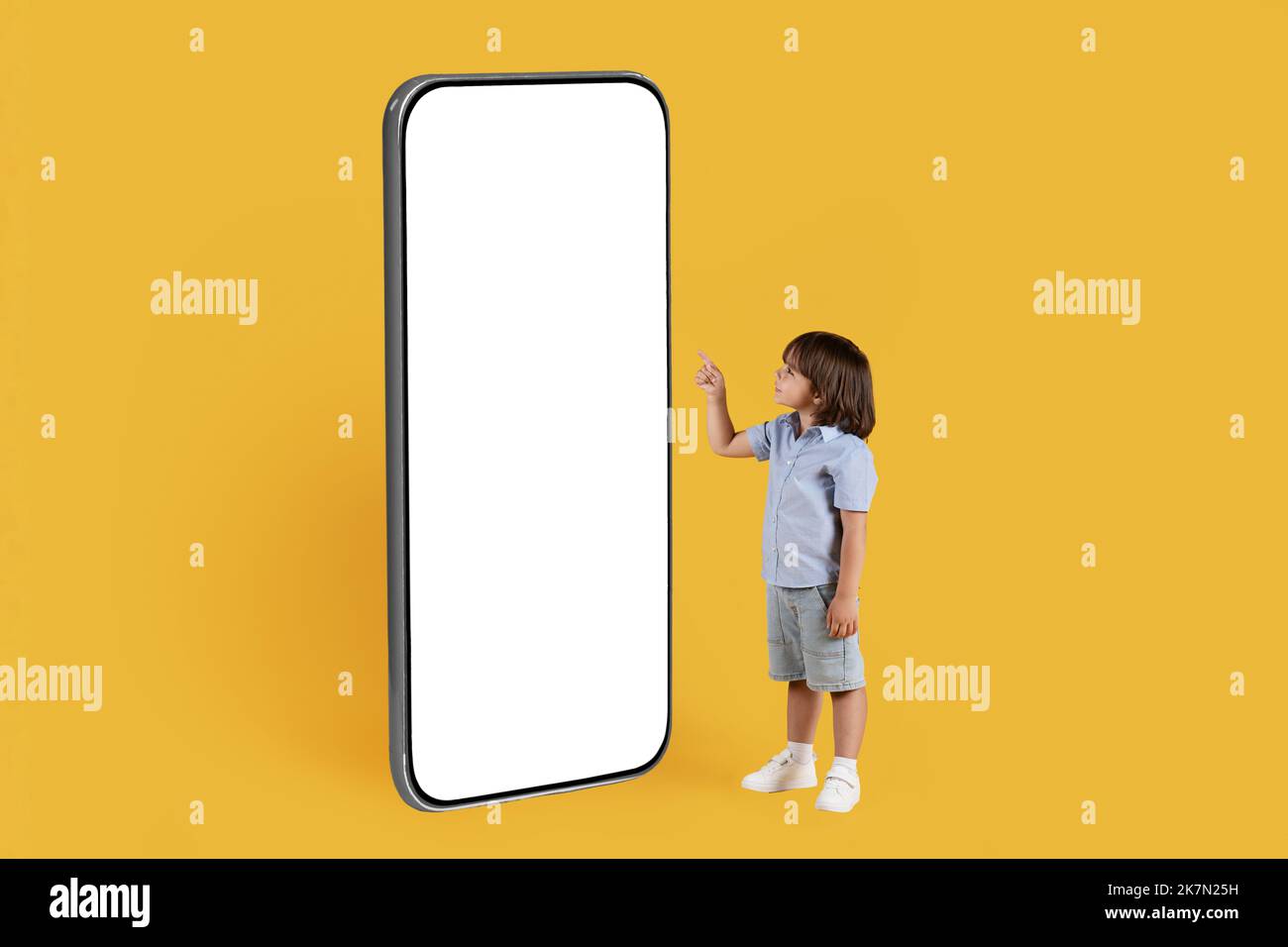 Adorable little boy pointing at big blank smartphone with white screen ...