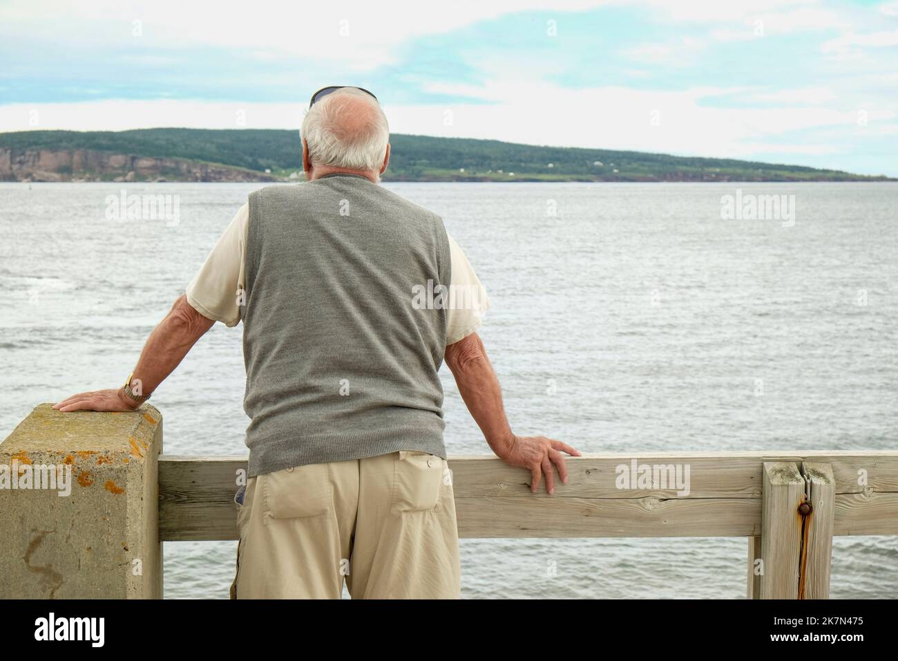 An old man gazing at a lake with hills in the background during daytime ...