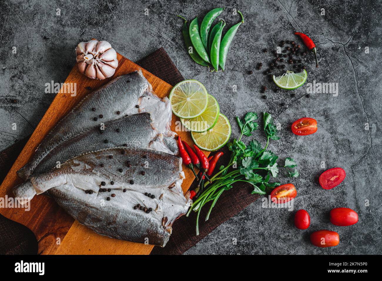 A top view of raw fresh fish on a wooden board, lime slices, garlic ...