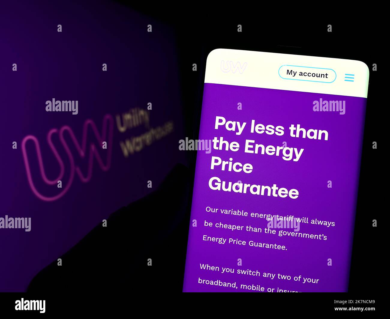 Person holding cellphone with webpage of British company Utility Warehouse (UW) on screen in ...