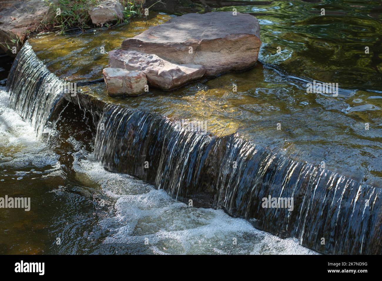 Water flowing over the rocky ledge of a garden pond Stock Photo - Alamy