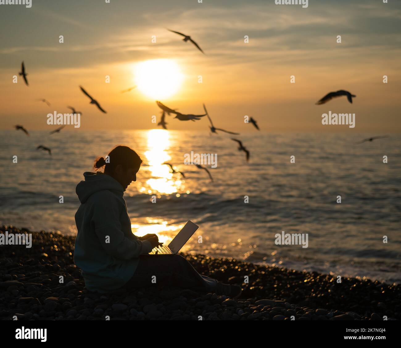 Caucasian woman typing on a laptop on the seashore at sunset. Freelance ...