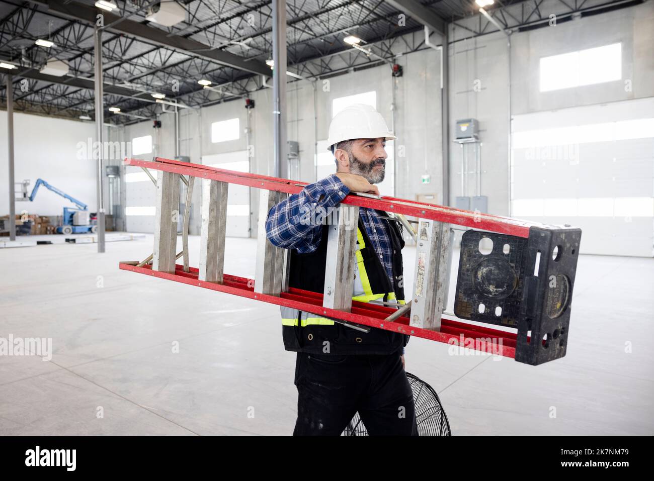 Construction worker carrying ladder in empty warehouse Stock Photo - Alamy