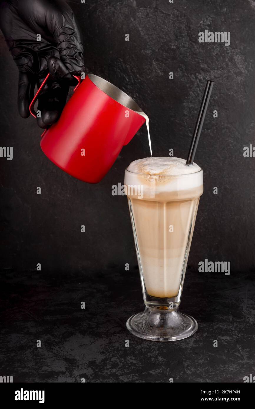 close-up of a barista preparing coffee with syrup and cream foam in a ...