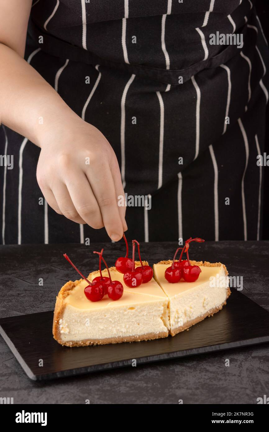 The chef decorates a classic cheesecake with cherry berries on a dark ...