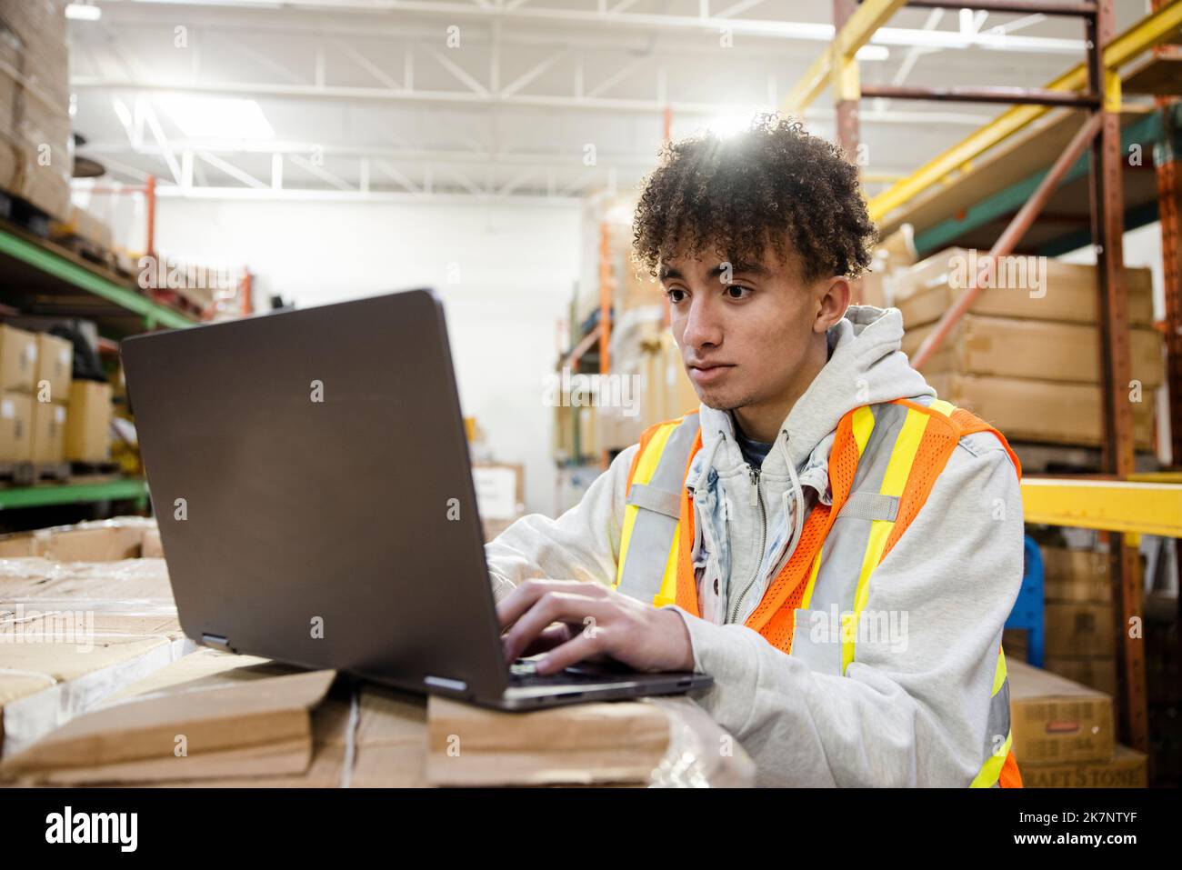 Teenage boy working at laptop in warehouse Stock Photo - Alamy