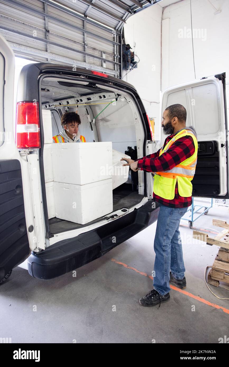 Male warehouse workers loading boxes into van at loading dock Stock ...
