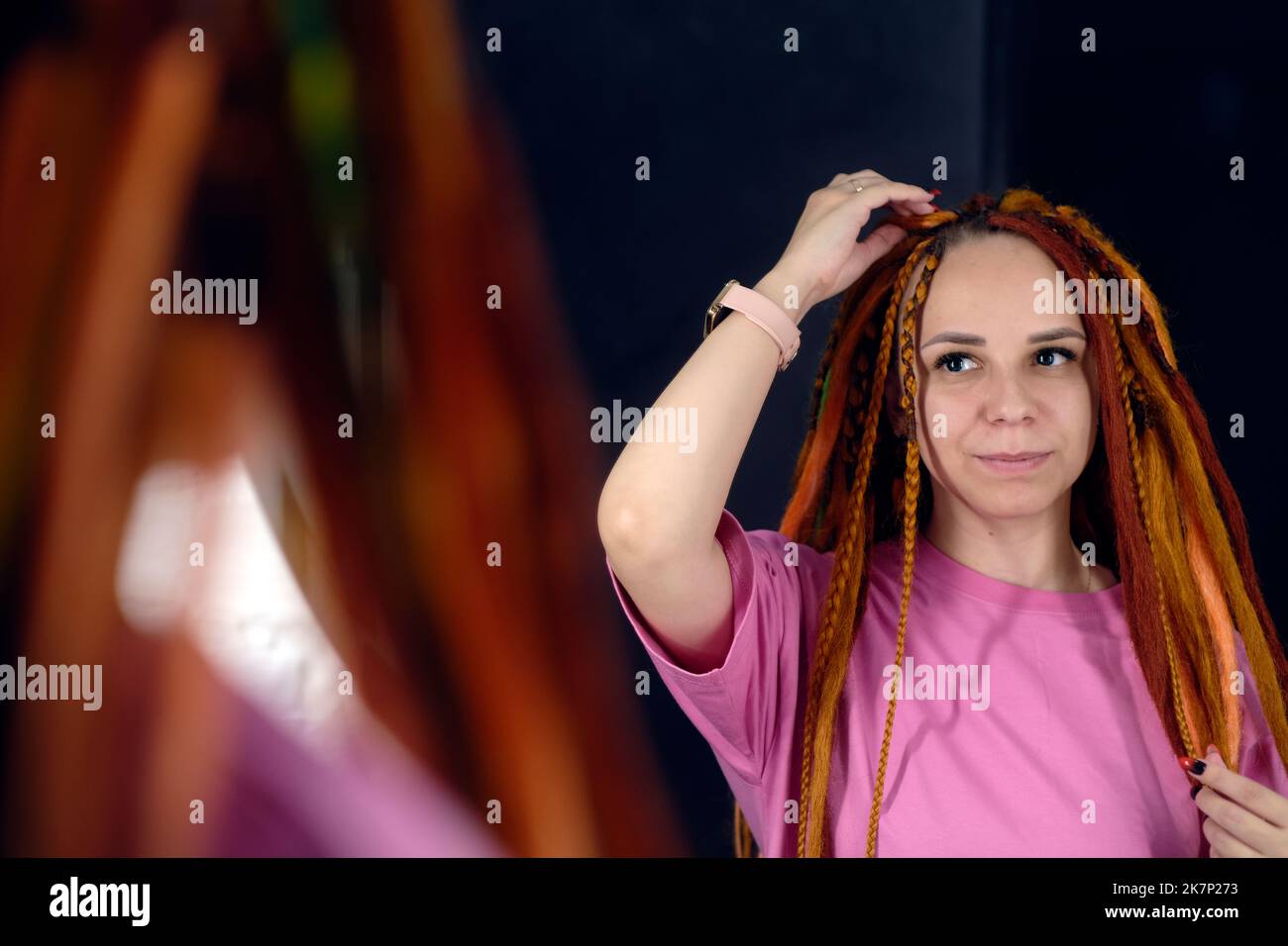 Young pretty woman with dreadlocks looking in mirror, preening ...