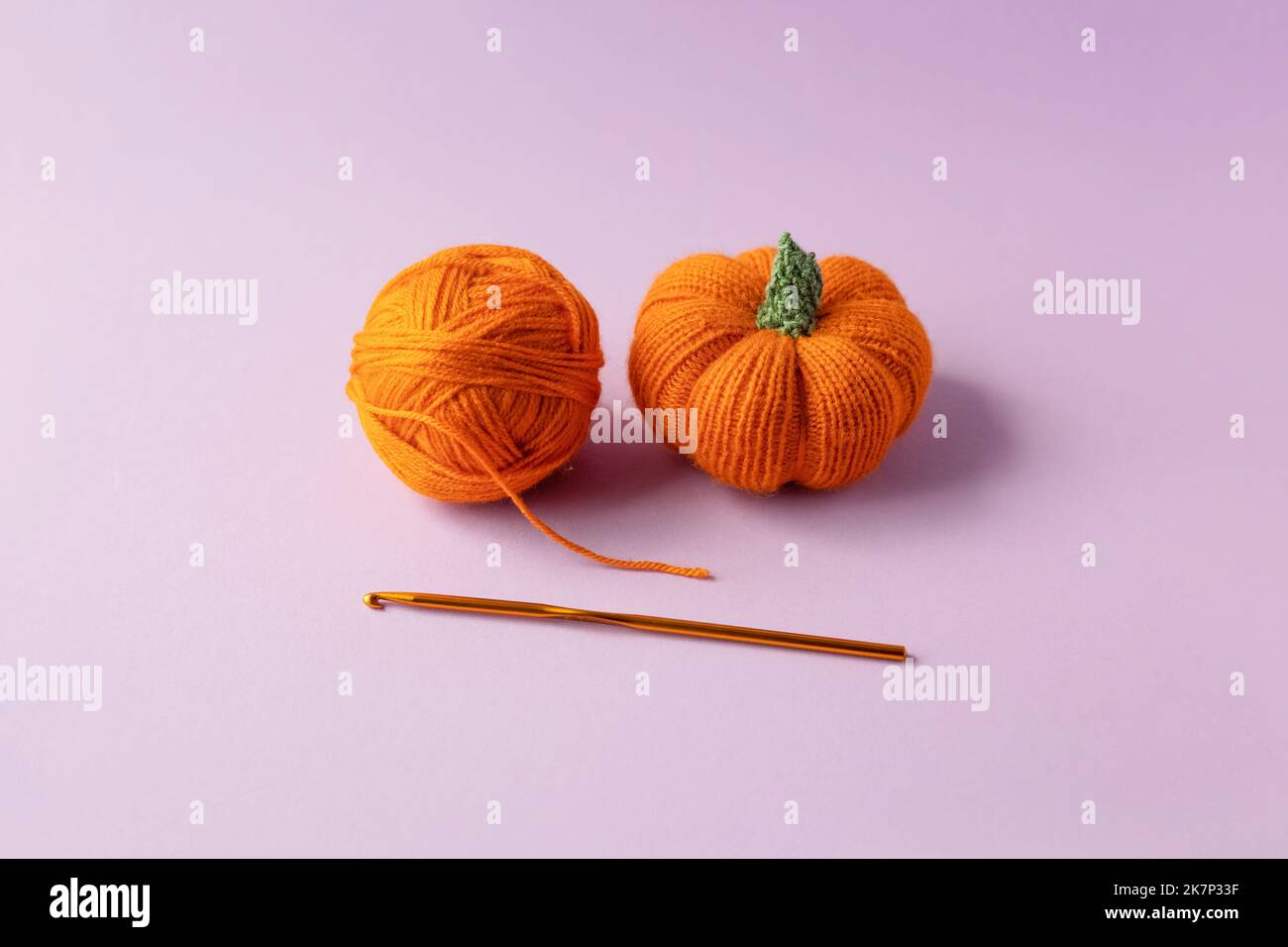 Knitted orange pumpkin and an orange ball of thread with a crochet hook ...