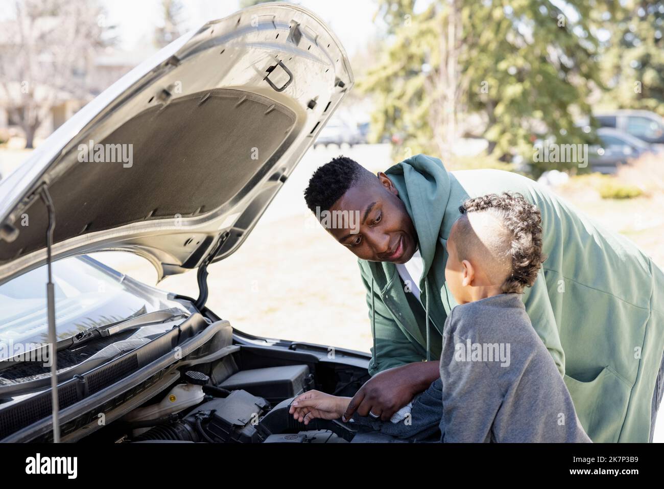 Father listening to son beside car engine with hood up in driveway ...