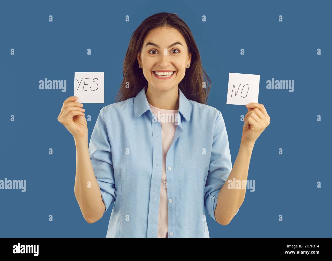 Doubted happy brunette woman with two cards yes and no looking at ...