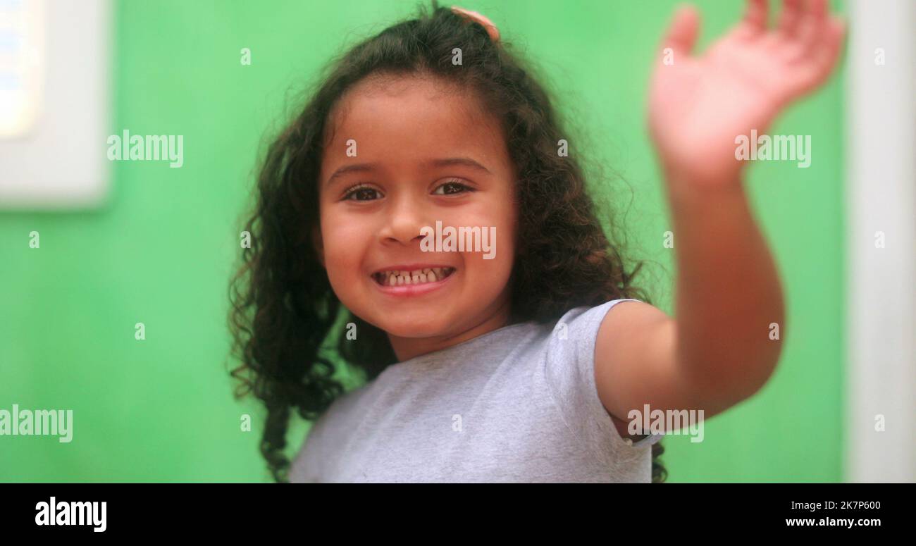 Hispanic little girl waving hello to camera. South american kid waves ...