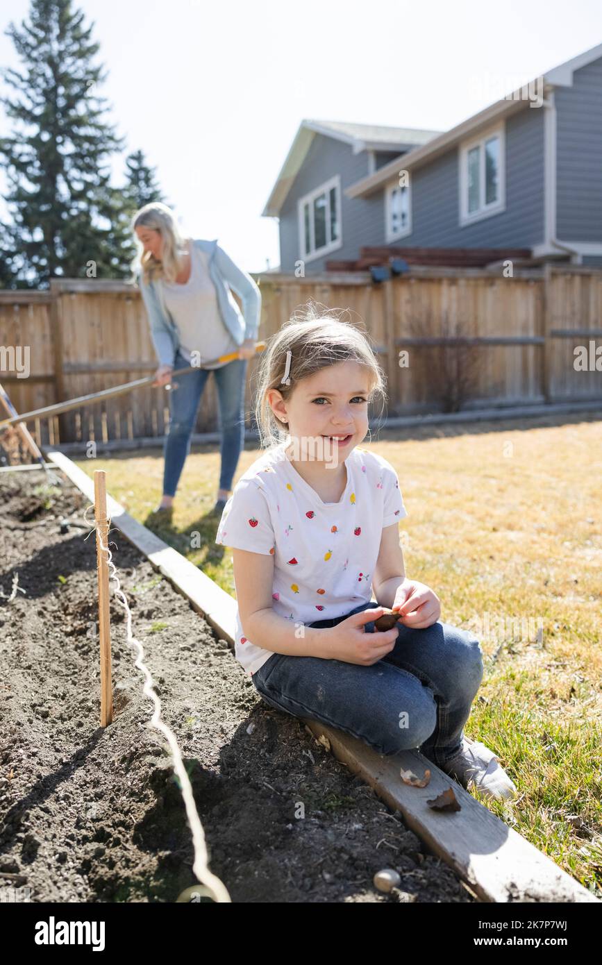 Portrait of cheerful girl sitting on flowerbed in backyard Stock Photo ...
