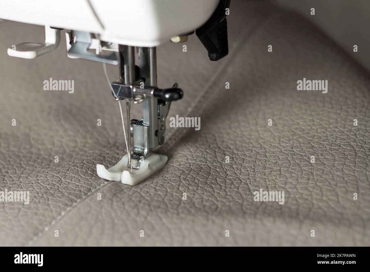 Modern sewing machine with special presser foot makes a seam on grey ...