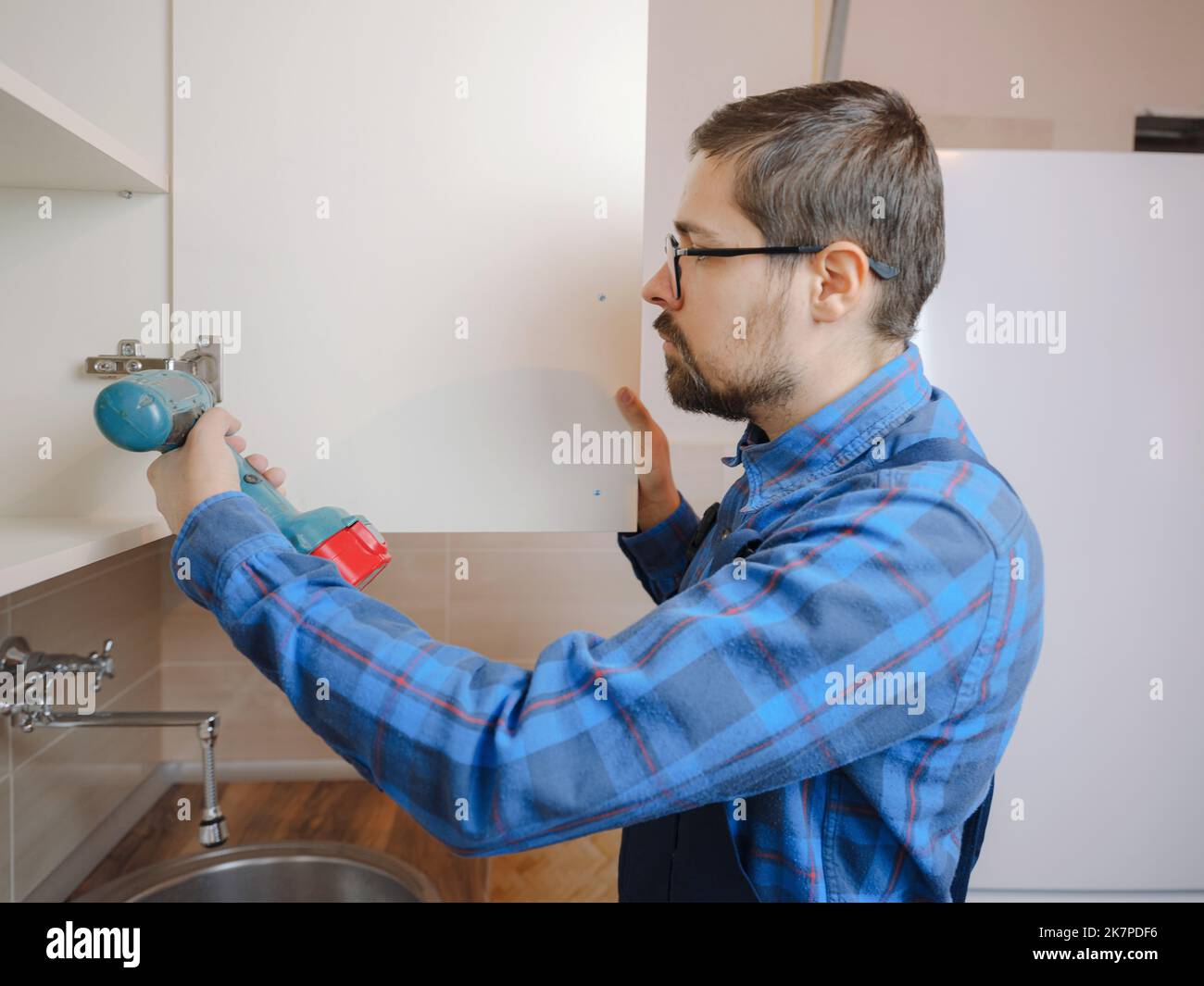 young man in blue work suit using electric screwdriver when assembling ...