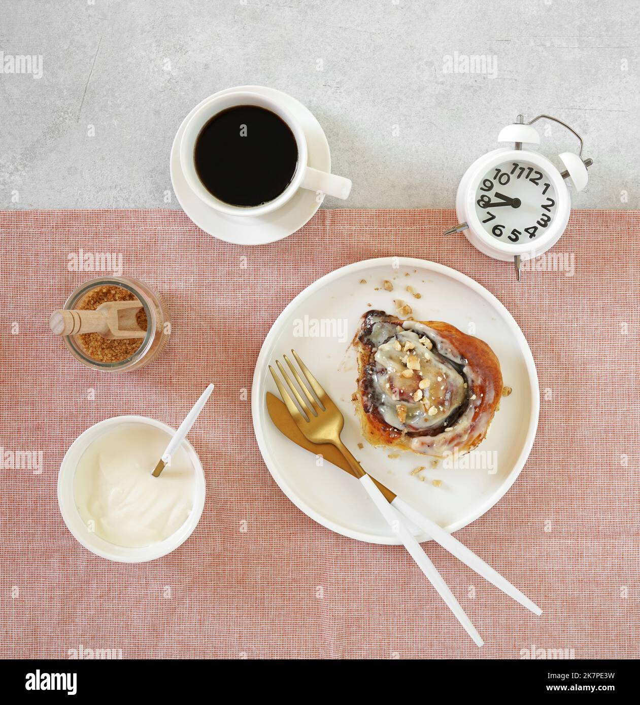 Cinnamon bun with cream on a plate with cup of coffee and alarm ...