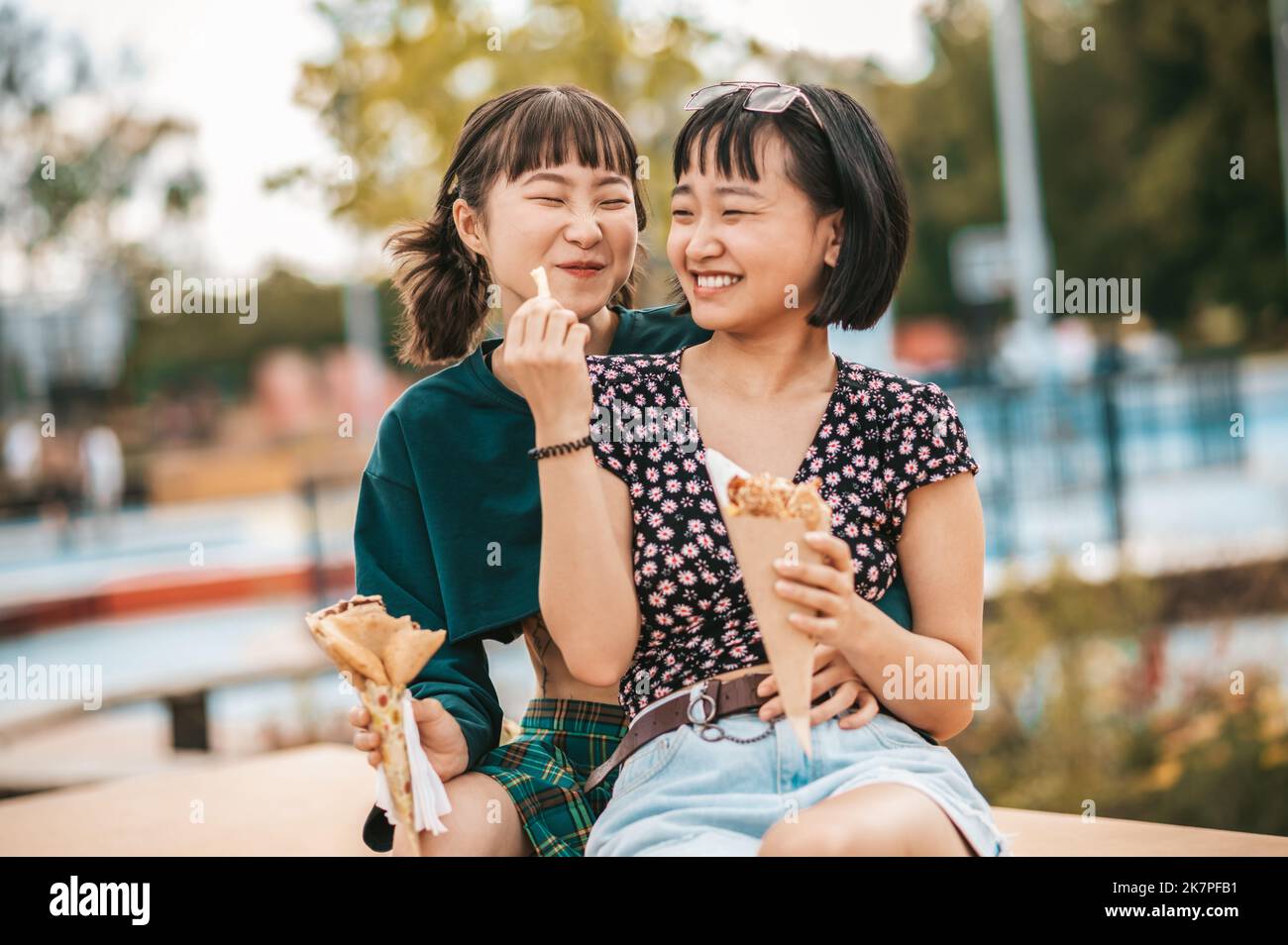 Enjoying street food. Two sweet girl eating outside and feeding each ...