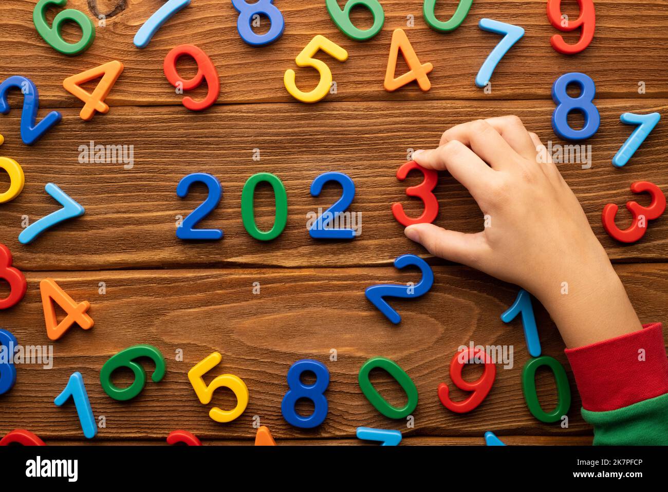 Child hand puts colored numbers 2023 new year on wooden background ...