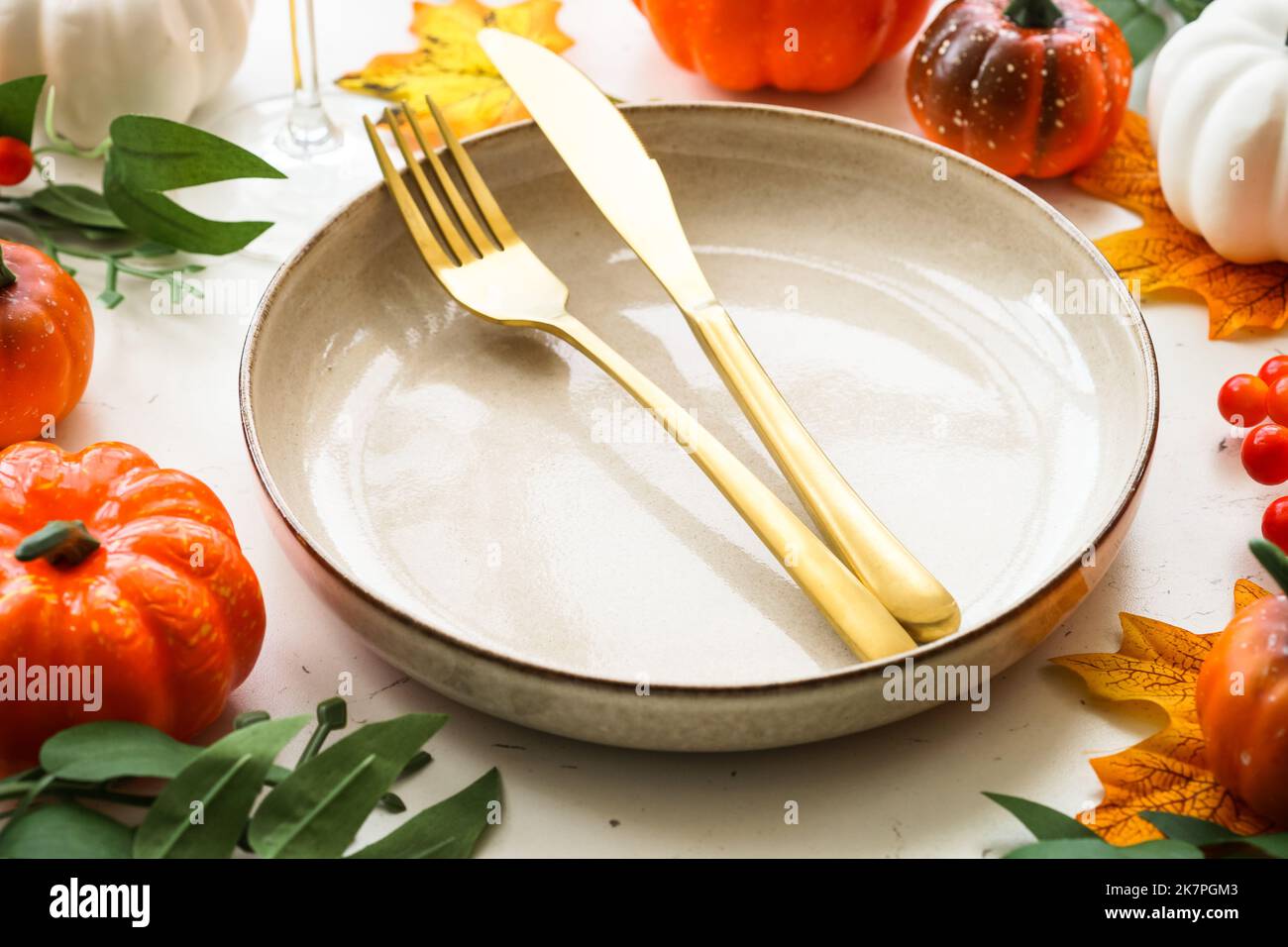 Autumn table setting. White plate, golden cutlery and fall decorations ...
