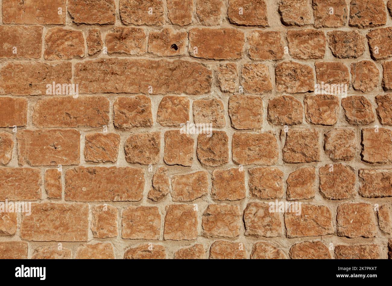 Front view of stone wall background. The stones are light orange in ...