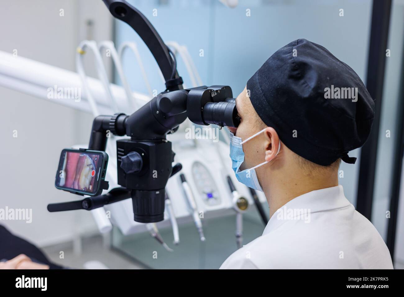A dentist and an assistant treat a patient's teeth using a microscope ...