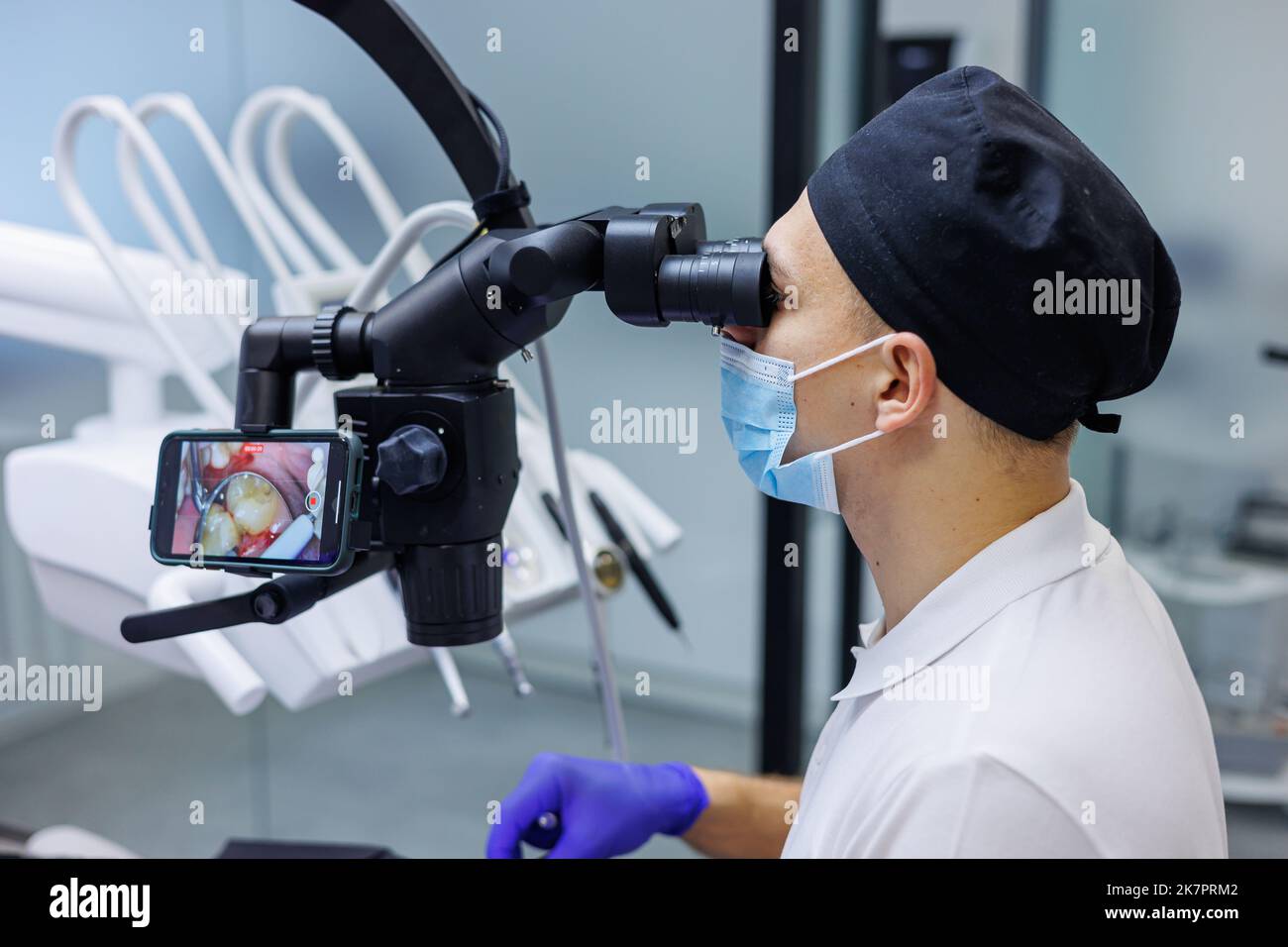 A dentist and an assistant treat a patient's teeth using a microscope ...