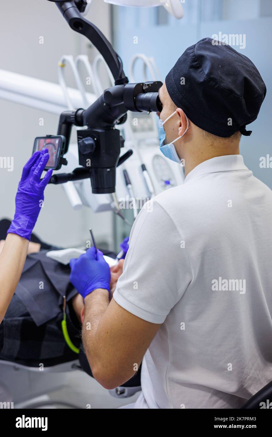A dentist and an assistant treat a patient's teeth using a microscope ...