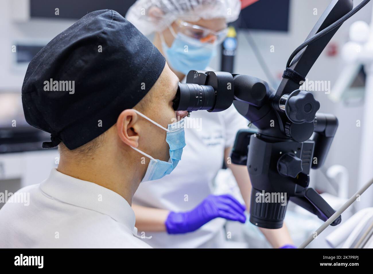 A dentist and an assistant treat a patient's teeth using a microscope ...