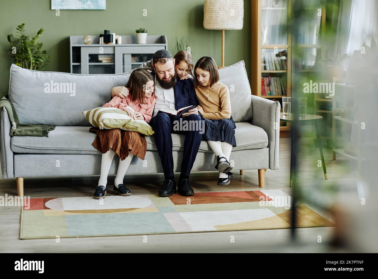 Full length portrait of orthodox Jewish father reading book to three ...