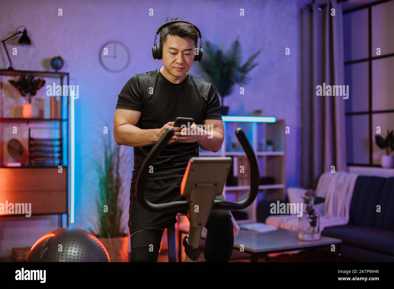 Healthy fit smiling asian man training at home on exercise static bike ...