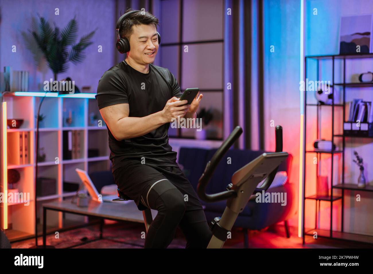 Healthy fit smiling asian man training at home on exercise static bike ...